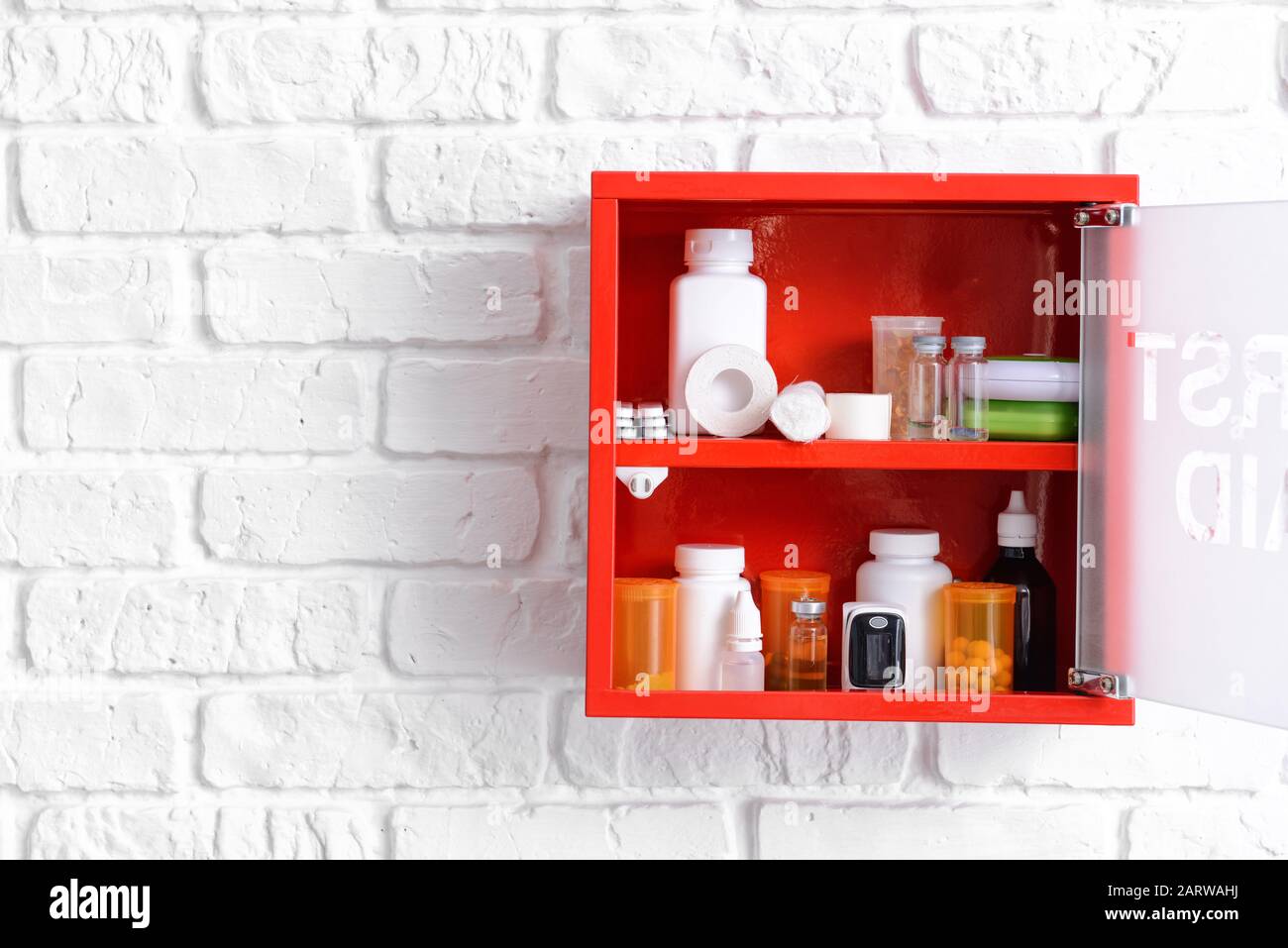 First aid kit hanging on white brick wall Stock Photo - Alamy