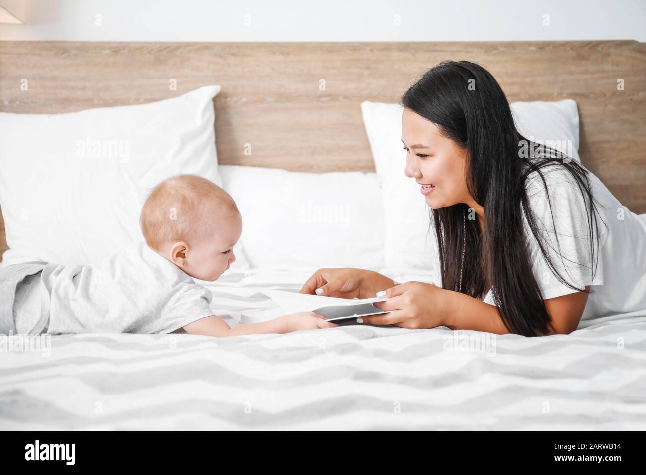 Asian mother and cute little baby reading book on bed Stock Photo - Alamy
