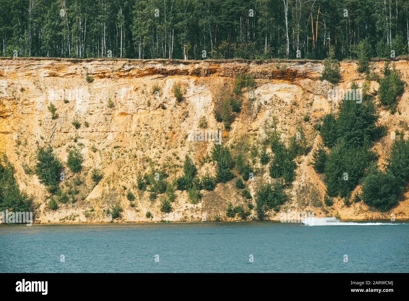 High rocky sandy steep bank covered with pine trees over a clear and ...