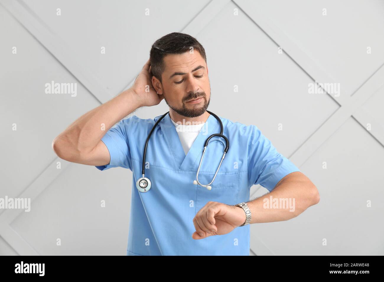 Portrait of male doctor looking at watch on light background Stock ...