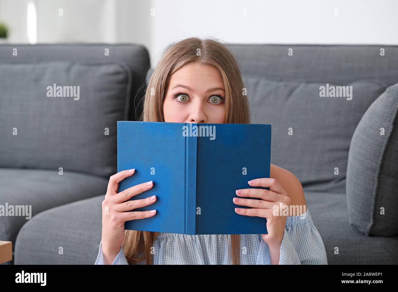 Shocked young woman reading book at home Stock Photo - Alamy
