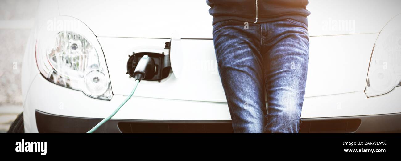 Man using mobile phone while charging electric car at charging station ...
