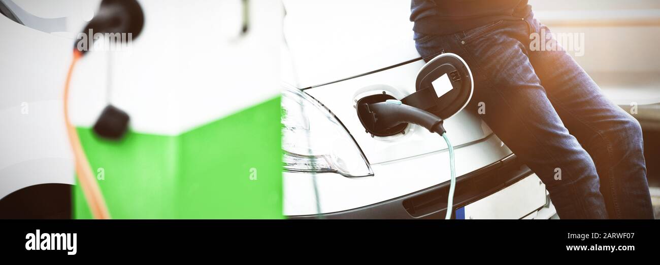 Man using mobile phone while charging electric car at charging station ...