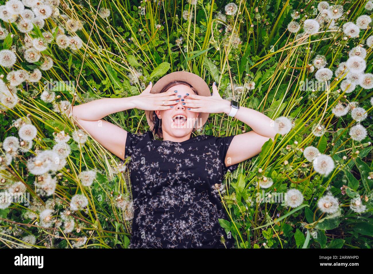 Young beautiful girl in sunglasses lies in dandelion field and shut her ...