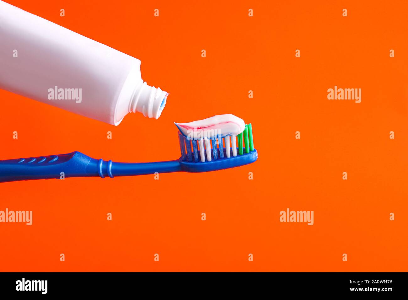 Squeezing of tooth paste from tube onto brush against color background ...