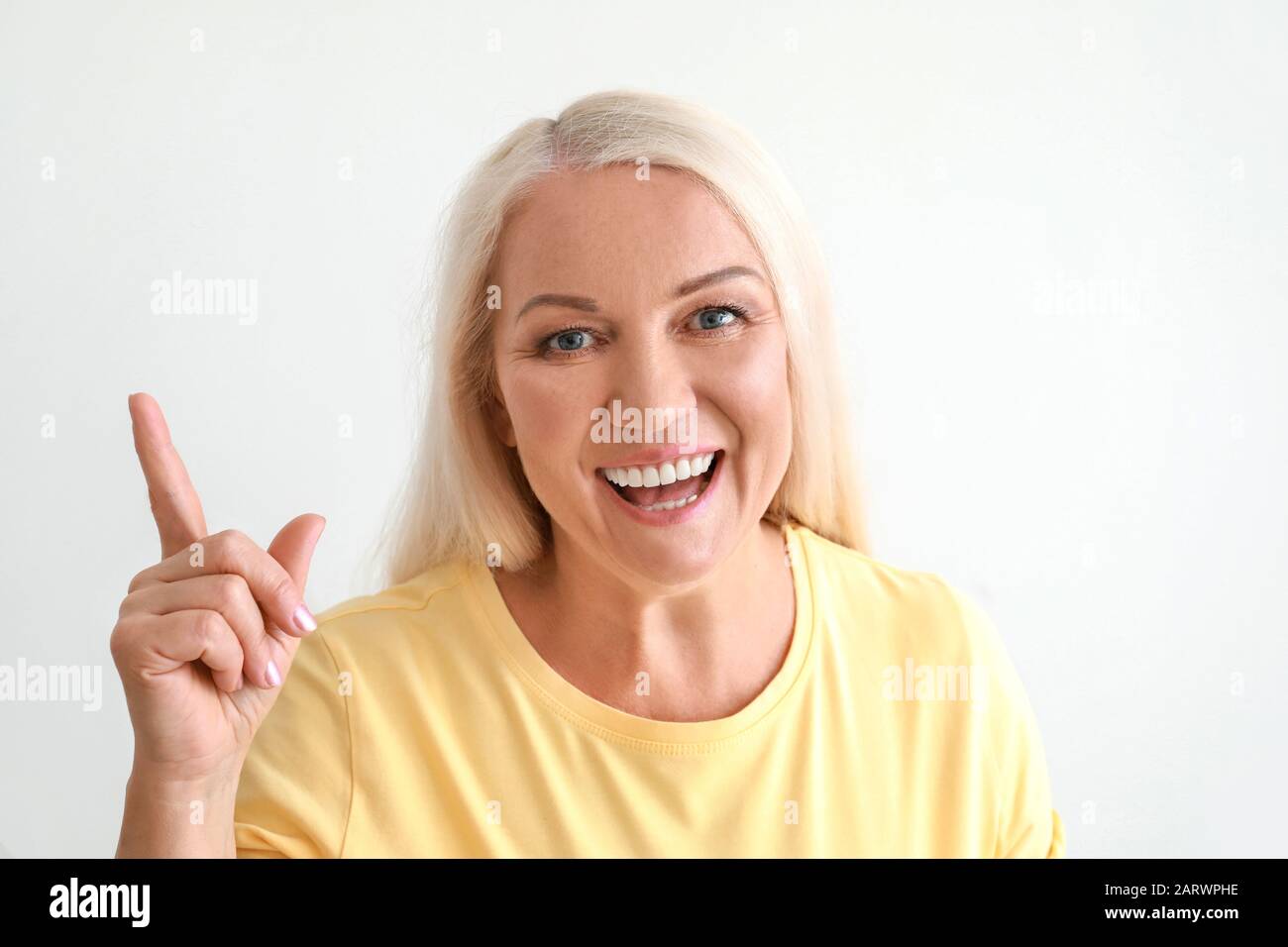 Portrait of beautiful mature woman with raised index finger on light ...