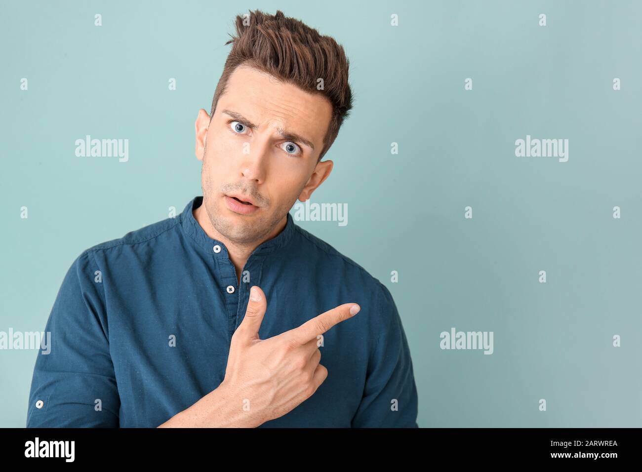 Surprised young man pointing at something on color background Stock ...
