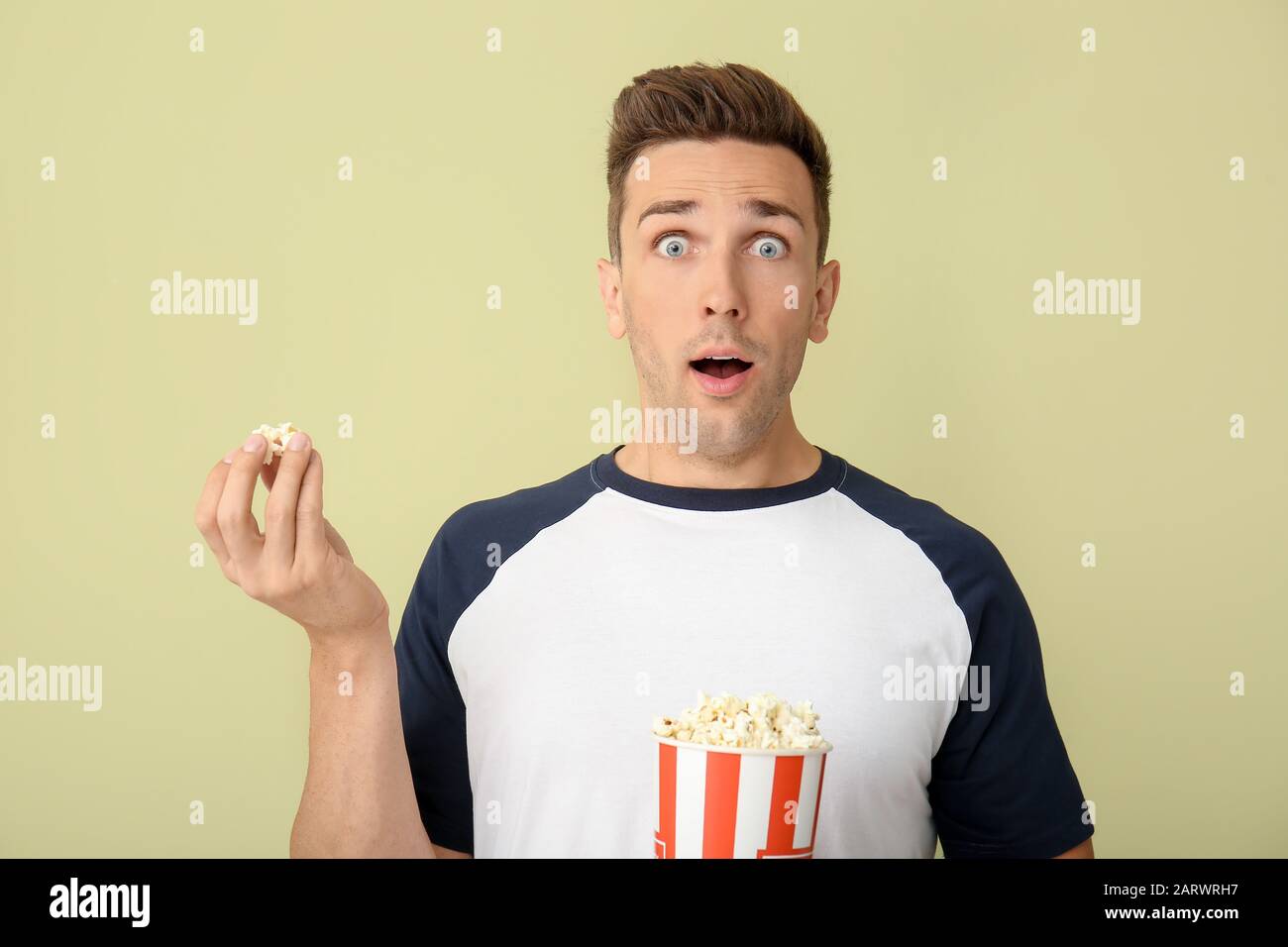 Shocked young man eating popcorn on color background Stock Photo - Alamy