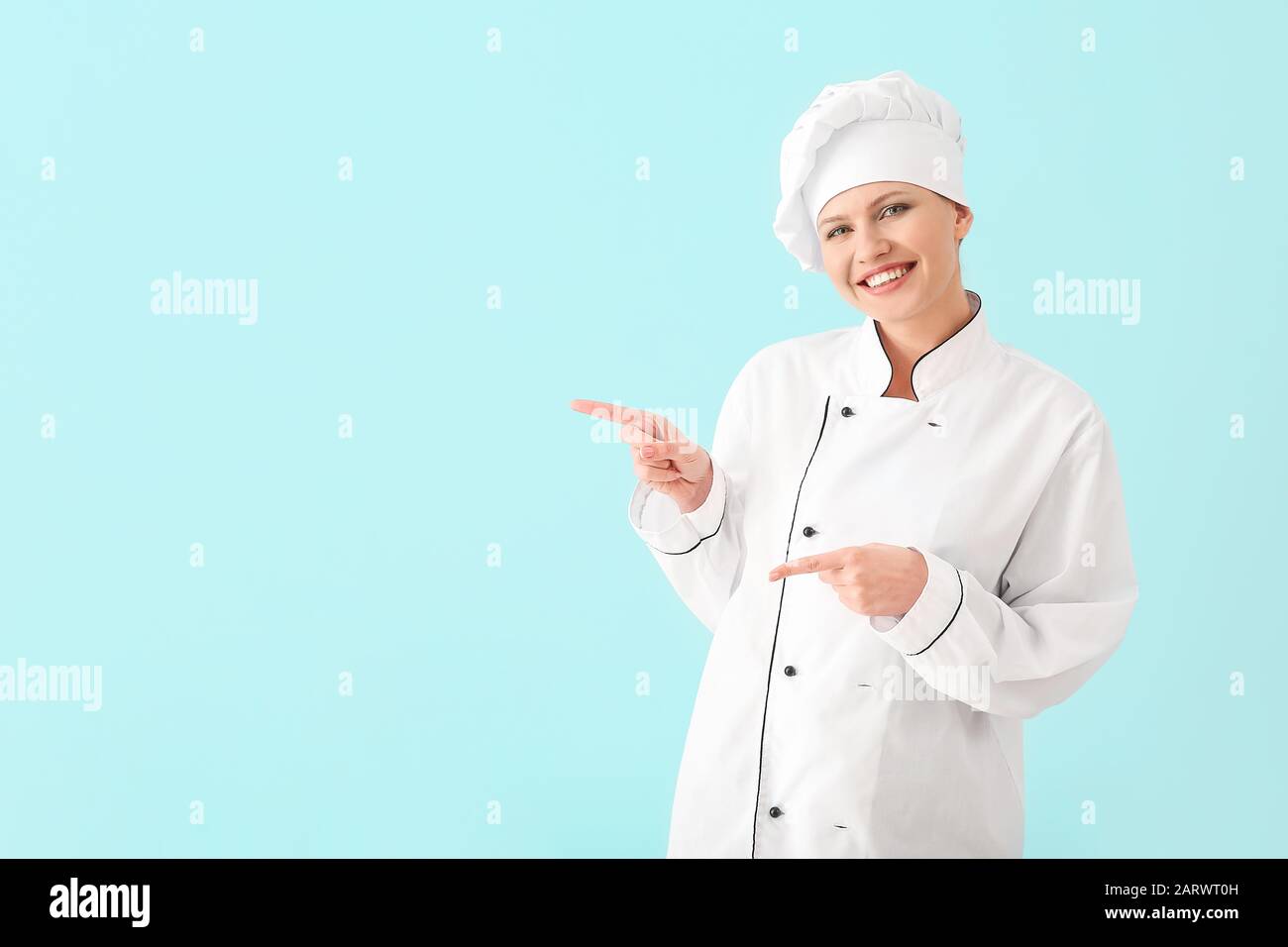 Beautiful female chef pointing at something on light background Stock ...
