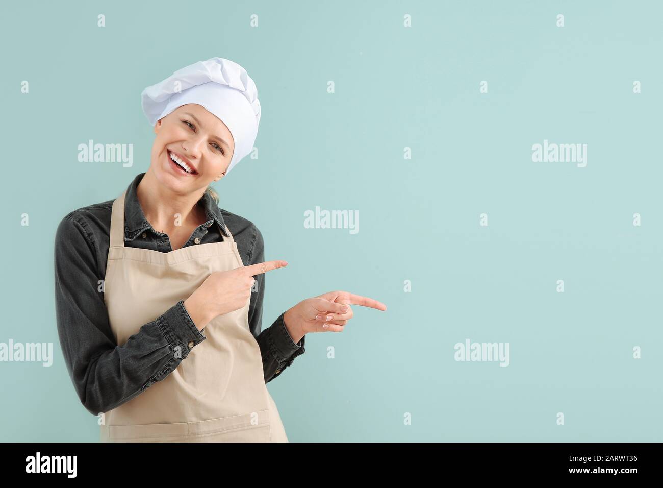Beautiful female chef pointing at something on color background Stock ...