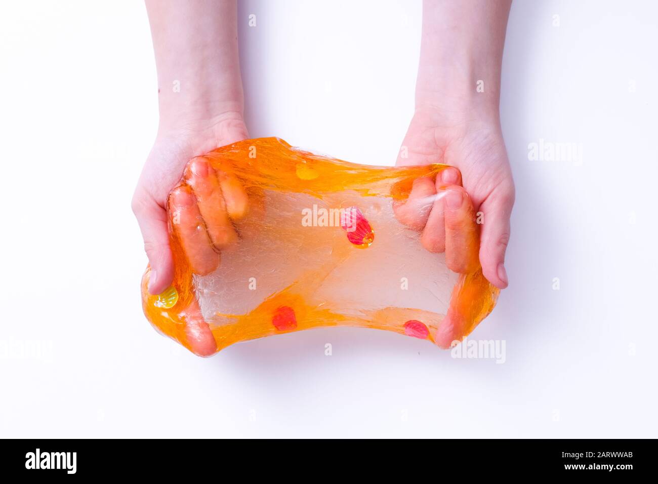 Girl stretching colorful orange slime to the sides. Kids hands playing ...