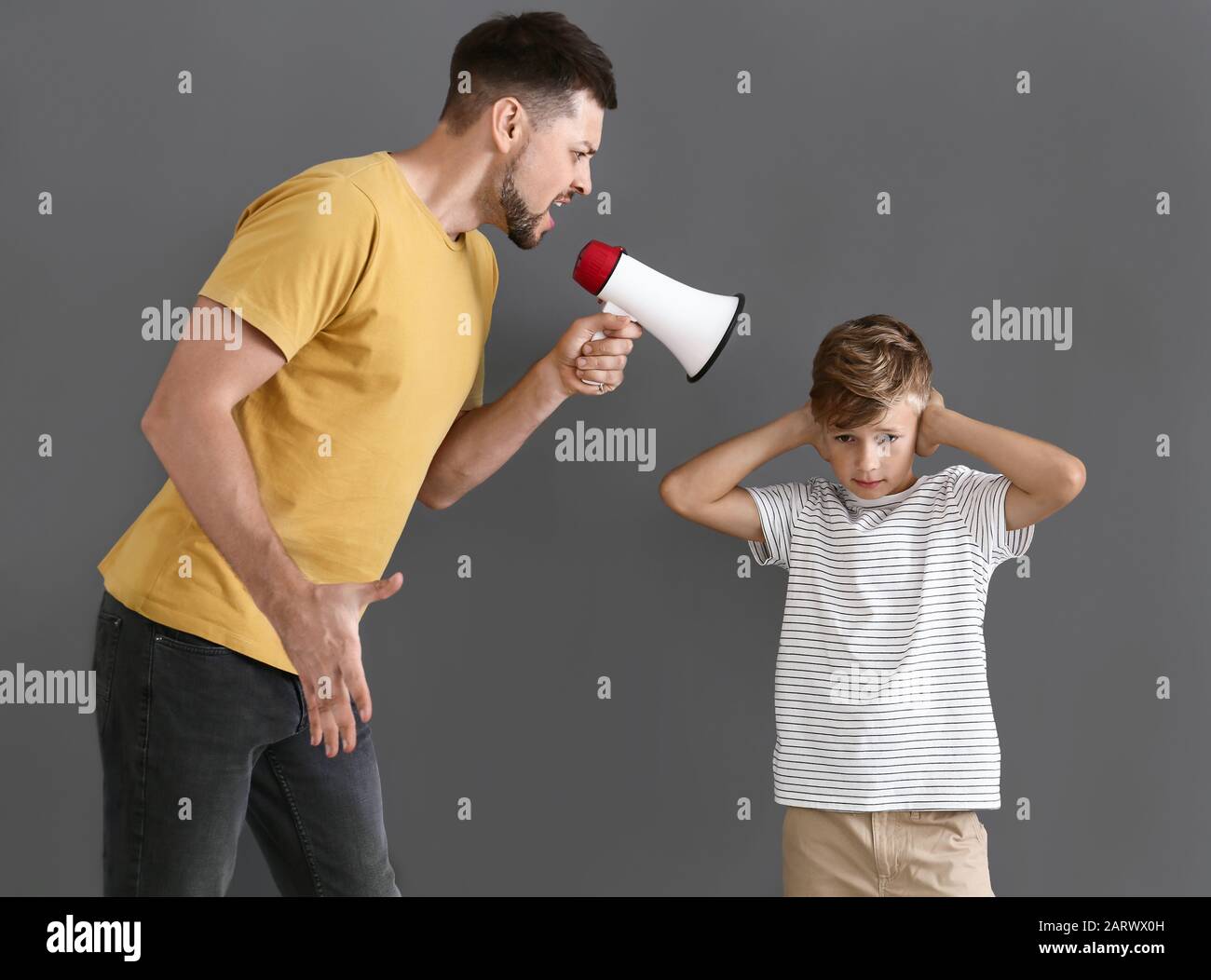 Little boy ignoring his angry father with megaphone against grey ...