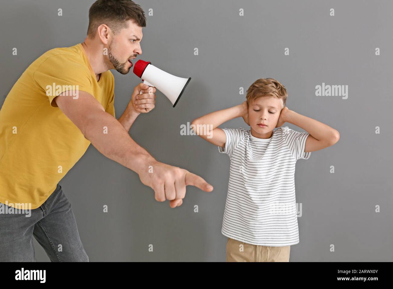 Little boy ignoring his angry father with megaphone against grey ...