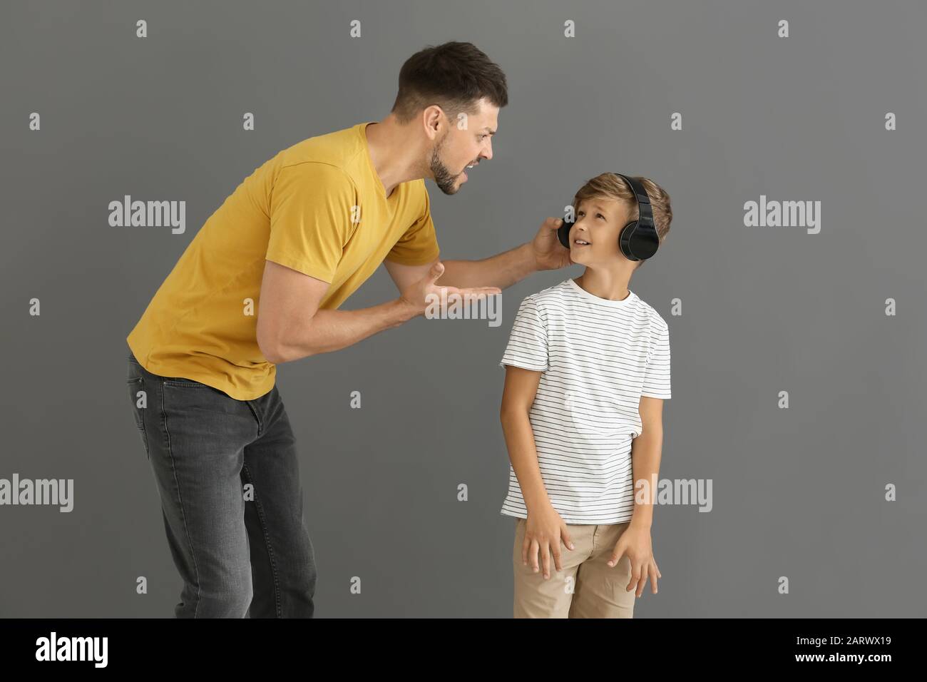 Little boy with headphones ignoring his angry father against grey ...