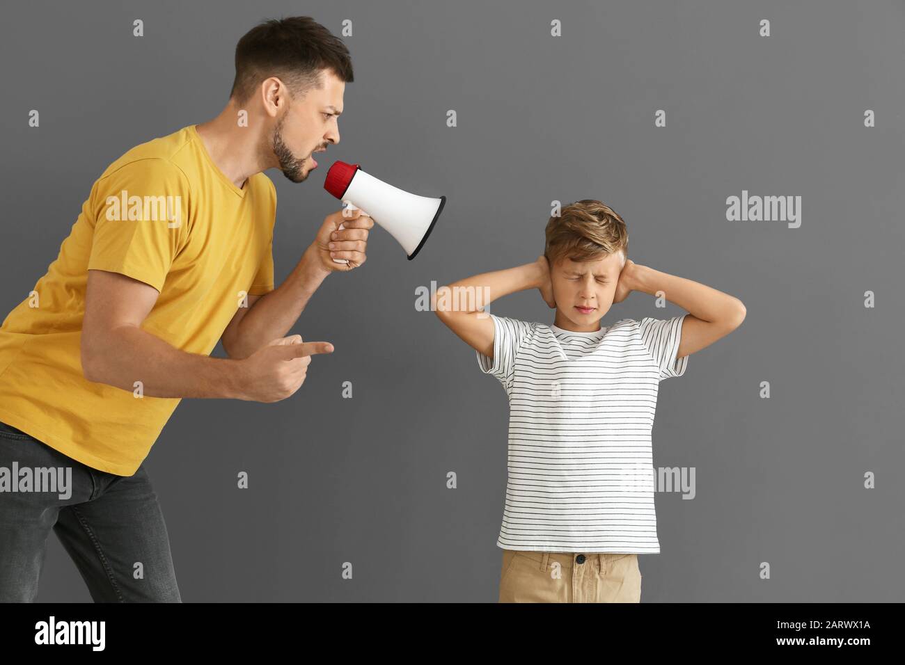 Little boy ignoring his angry father with megaphone against grey ...
