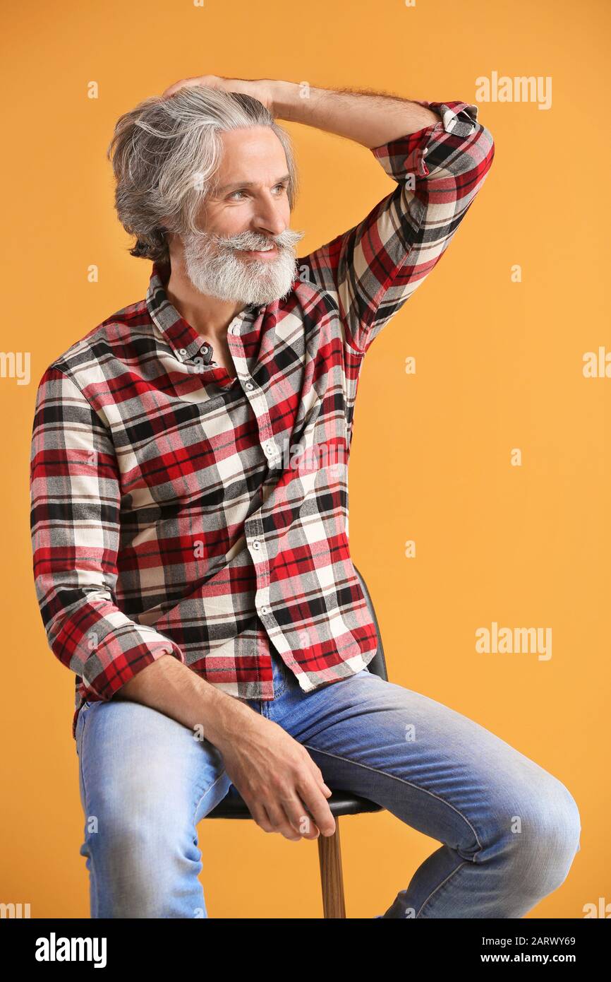 Portrait of handsome senior man sitting on chair against color ...