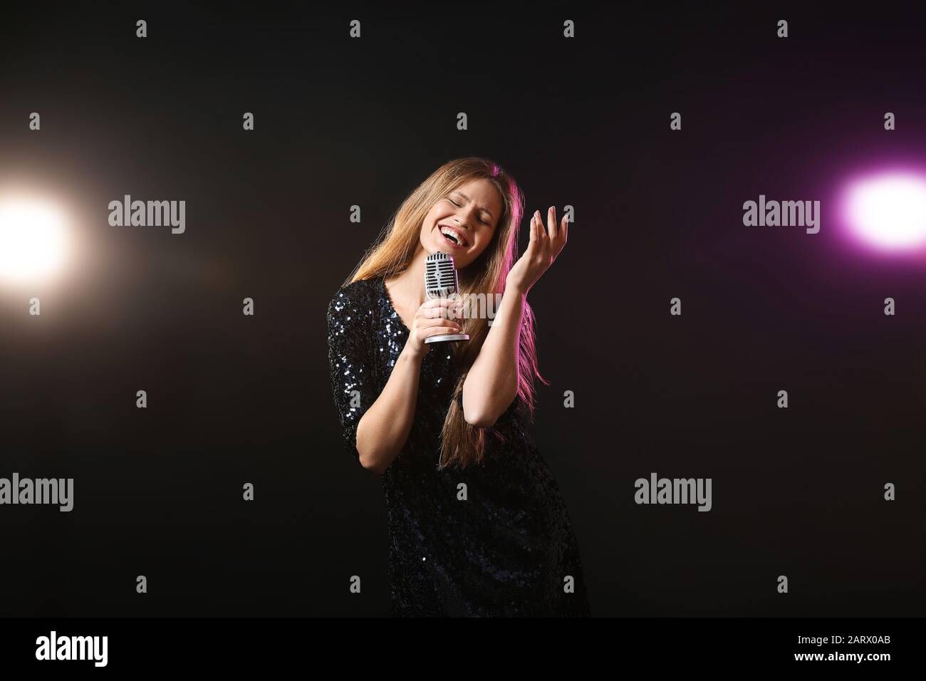 Beautiful young female singer with microphone on stage Stock Photo - Alamy