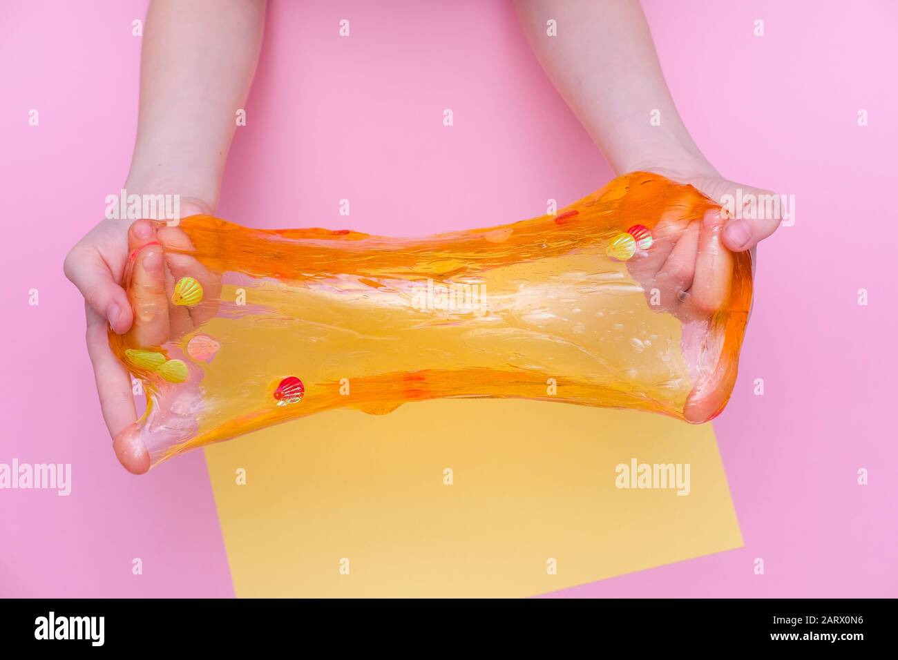 Girl stretching colorful orange slime to the sides. Kids hands playing ...