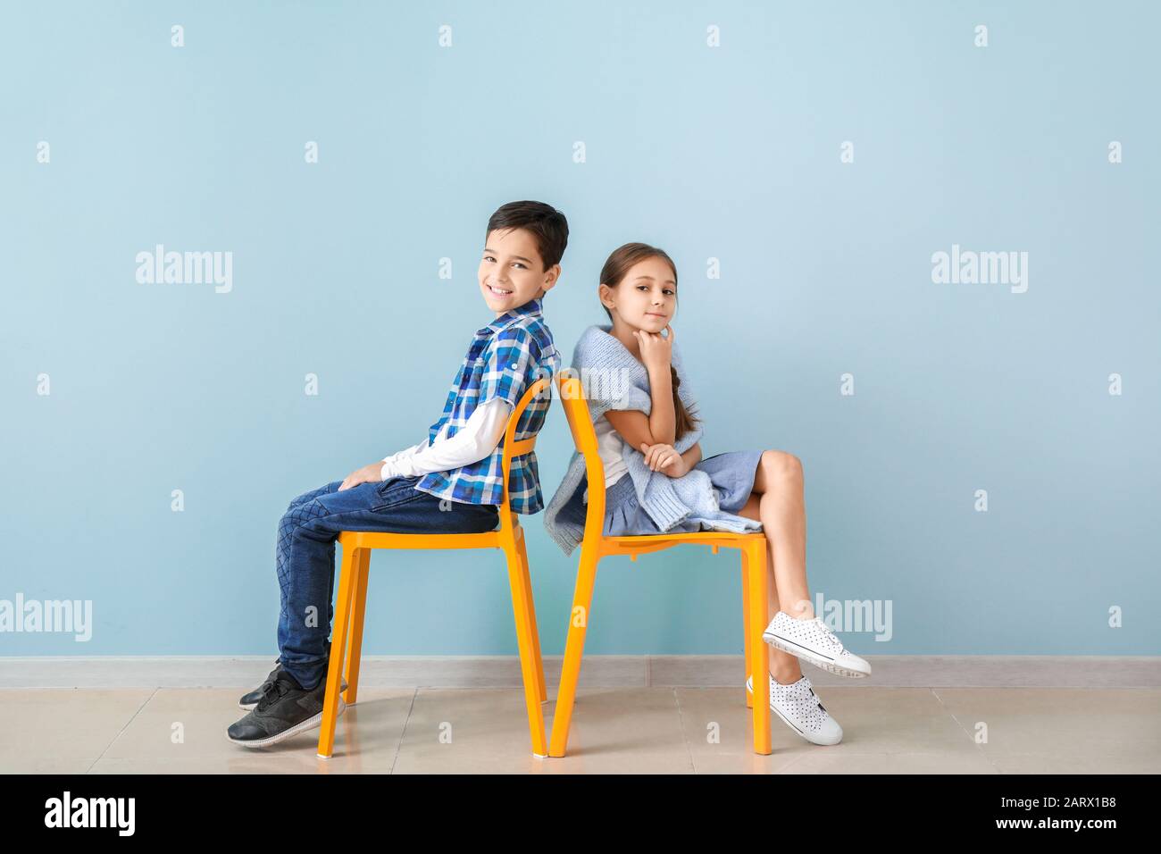 Cute fashionable children sitting on chairs near color wall Stock Photo ...