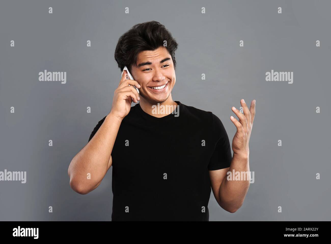 Portrait of handsome Asian man talking by phone on grey background ...