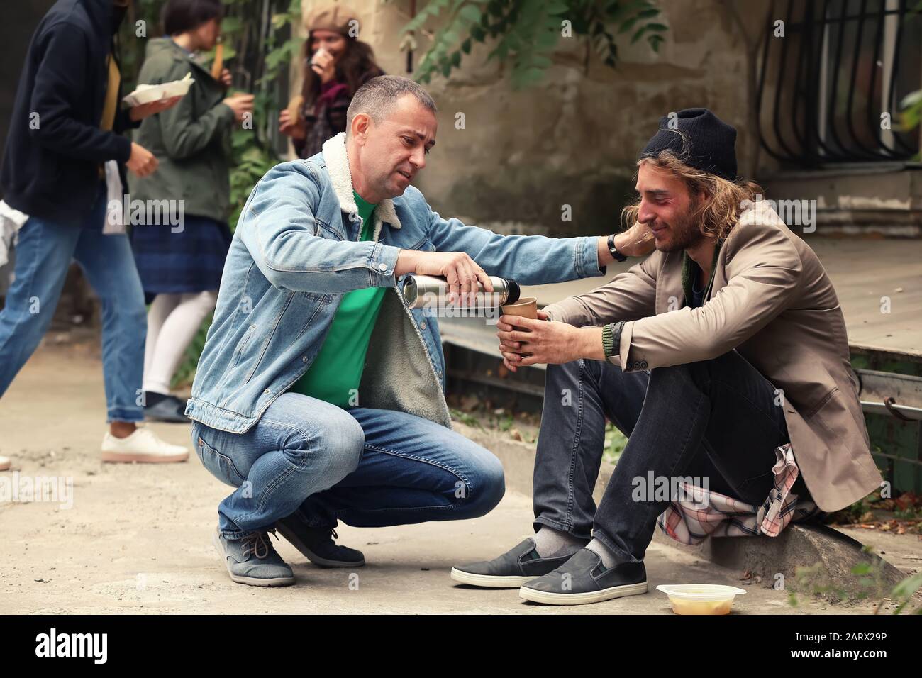 Volunteer giving drink to homeless man outdoors Stock Photo - Alamy