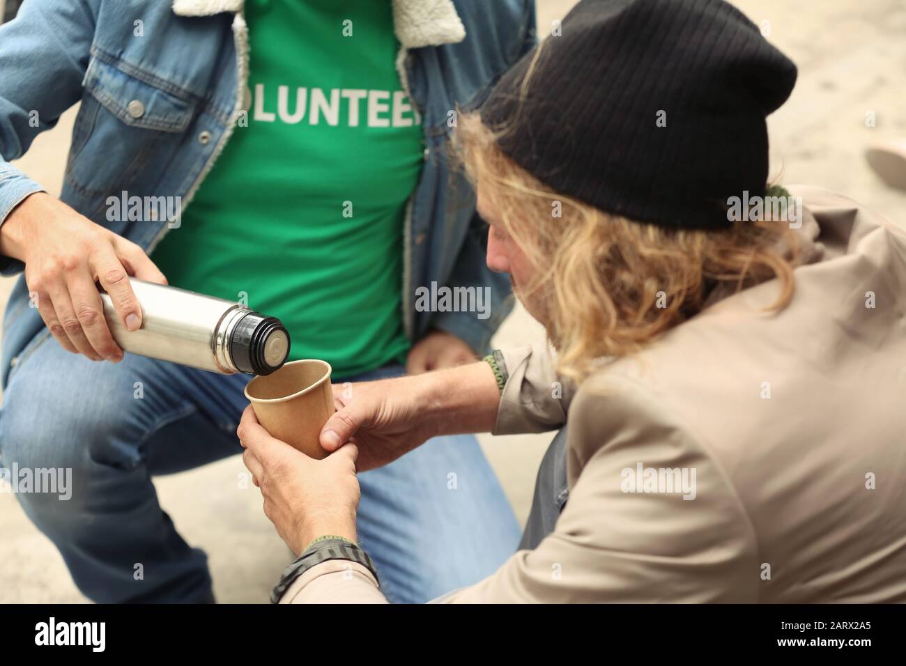 Volunteer giving drink to homeless man outdoors Stock Photo - Alamy