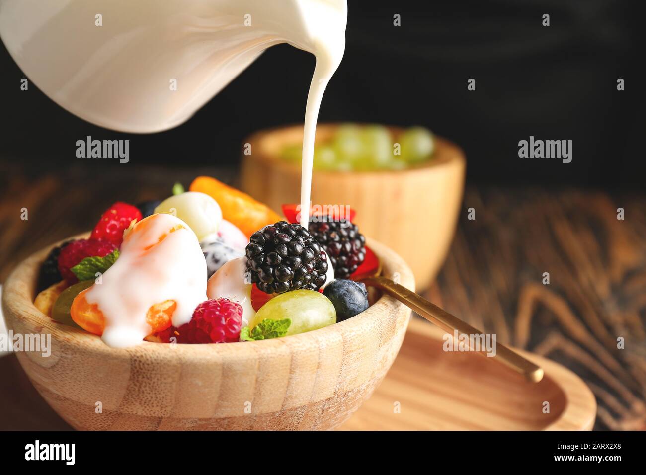 Pouring of yogurt from jug onto tasty fruit salad, closeup Stock Photo ...