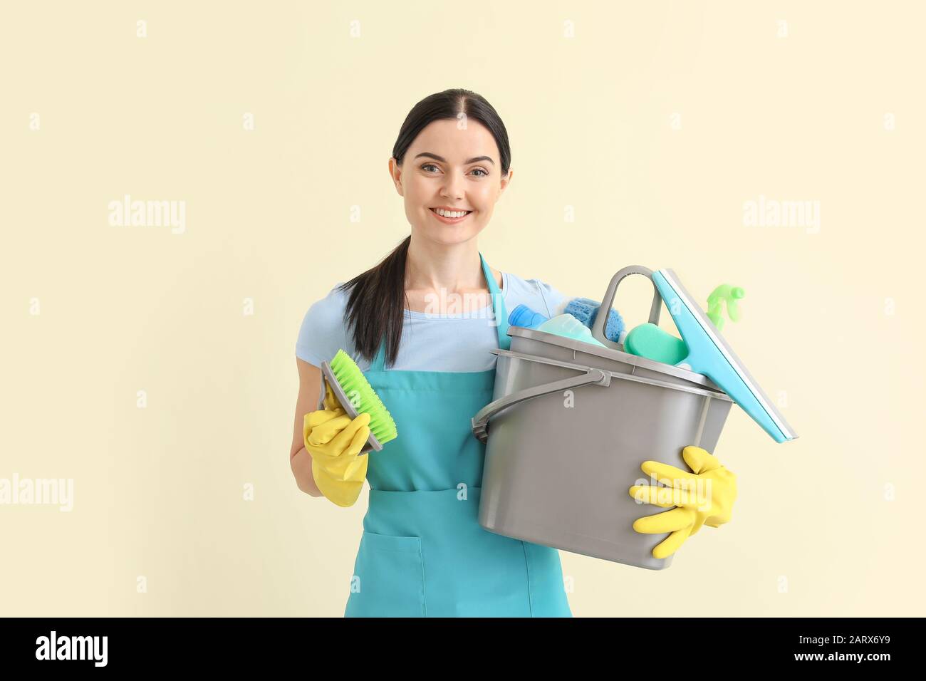Female janitor with cleaning supplies on light background Stock Photo ...