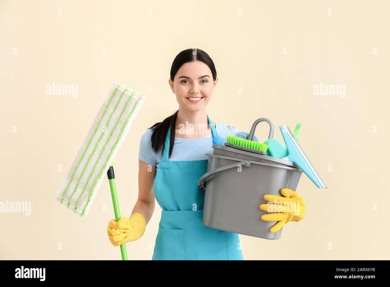 Female janitor with cleaning supplies on light background Stock Photo ...