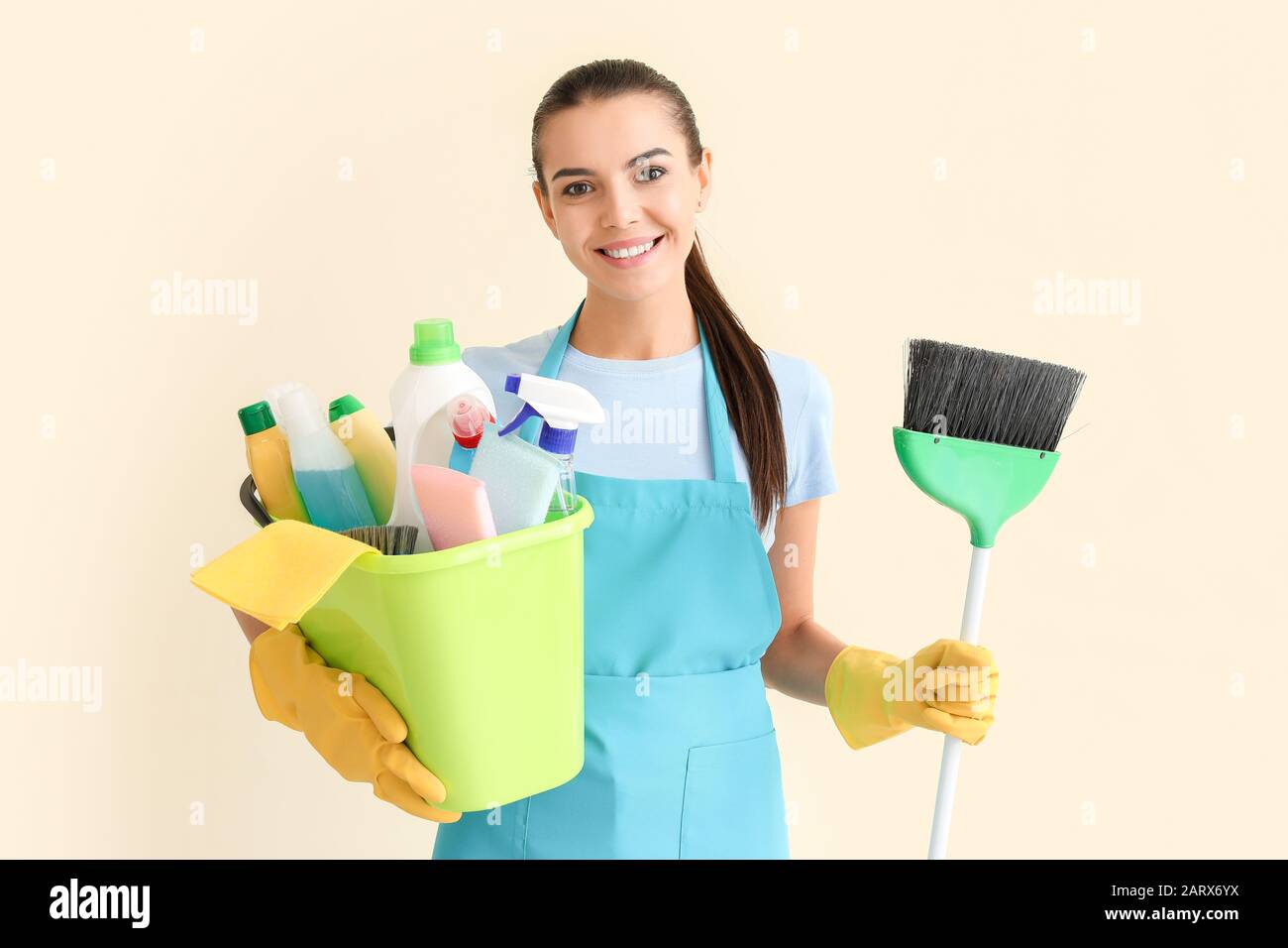 Female janitor with cleaning supplies on light background Stock Photo ...