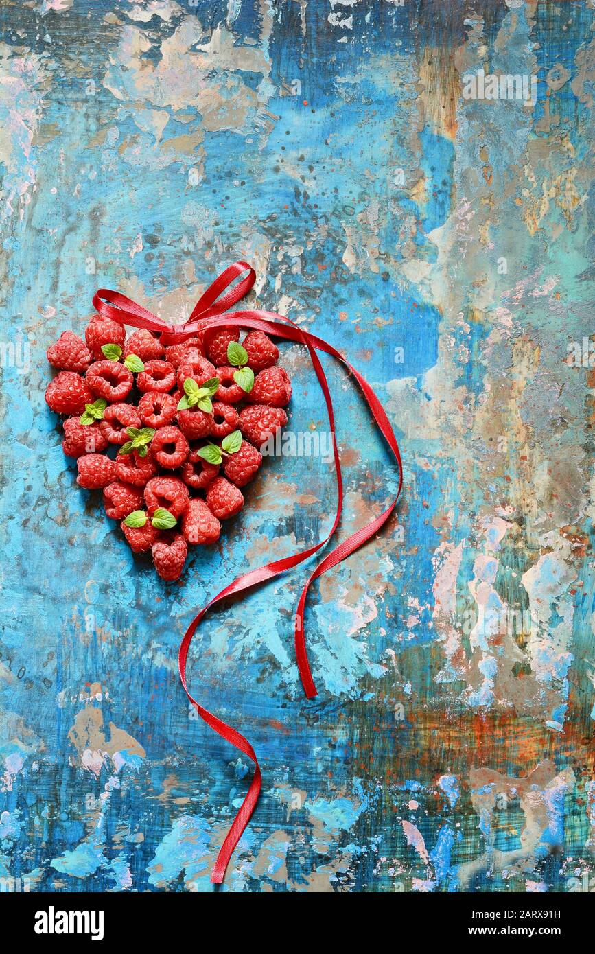 Heart shape made of premium raspberries on a blue background. Close up ...