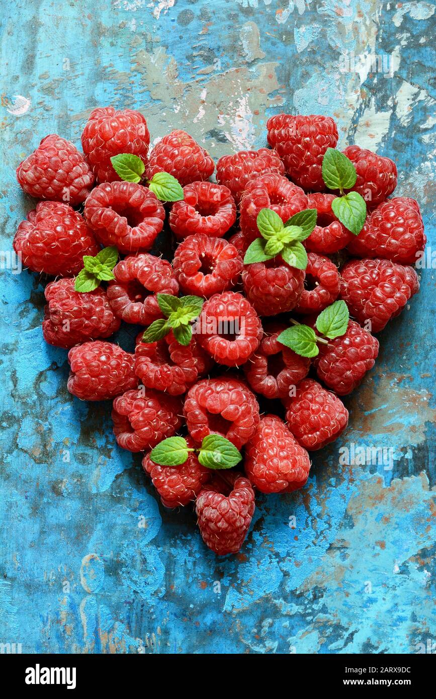 Heart shape made of premium raspberries on a blue background. Close up ...