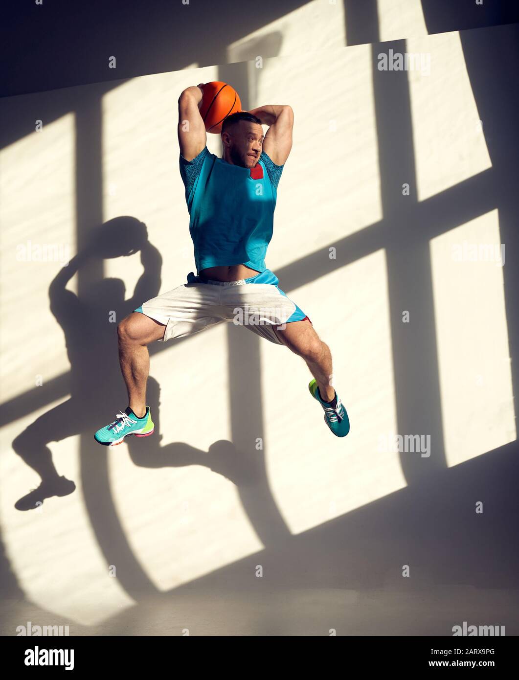 Young athletic basketball player jumping with ball in front of wall ...