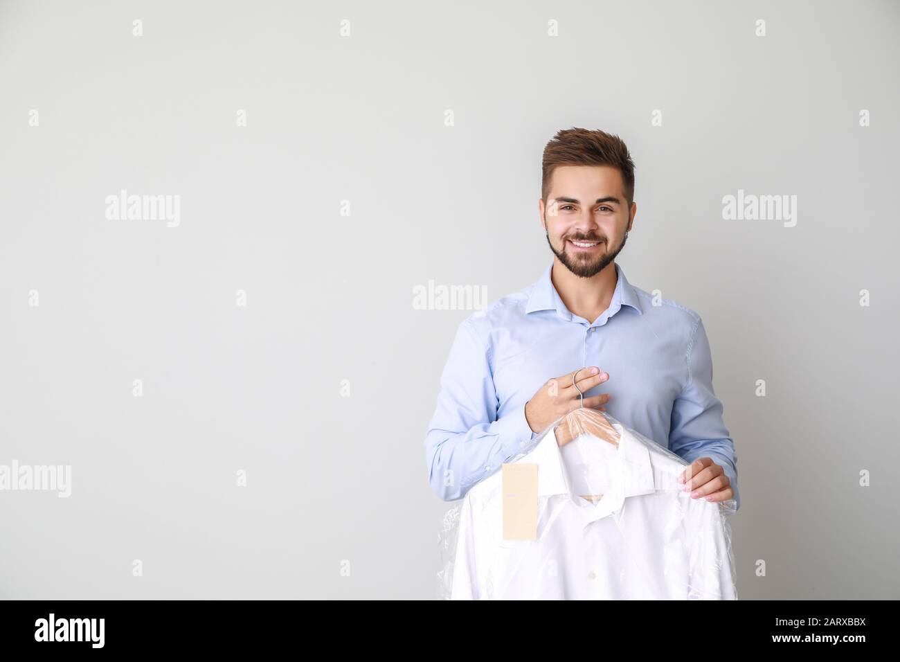 Male worker of modern dry-cleaner with clothes on light background ...