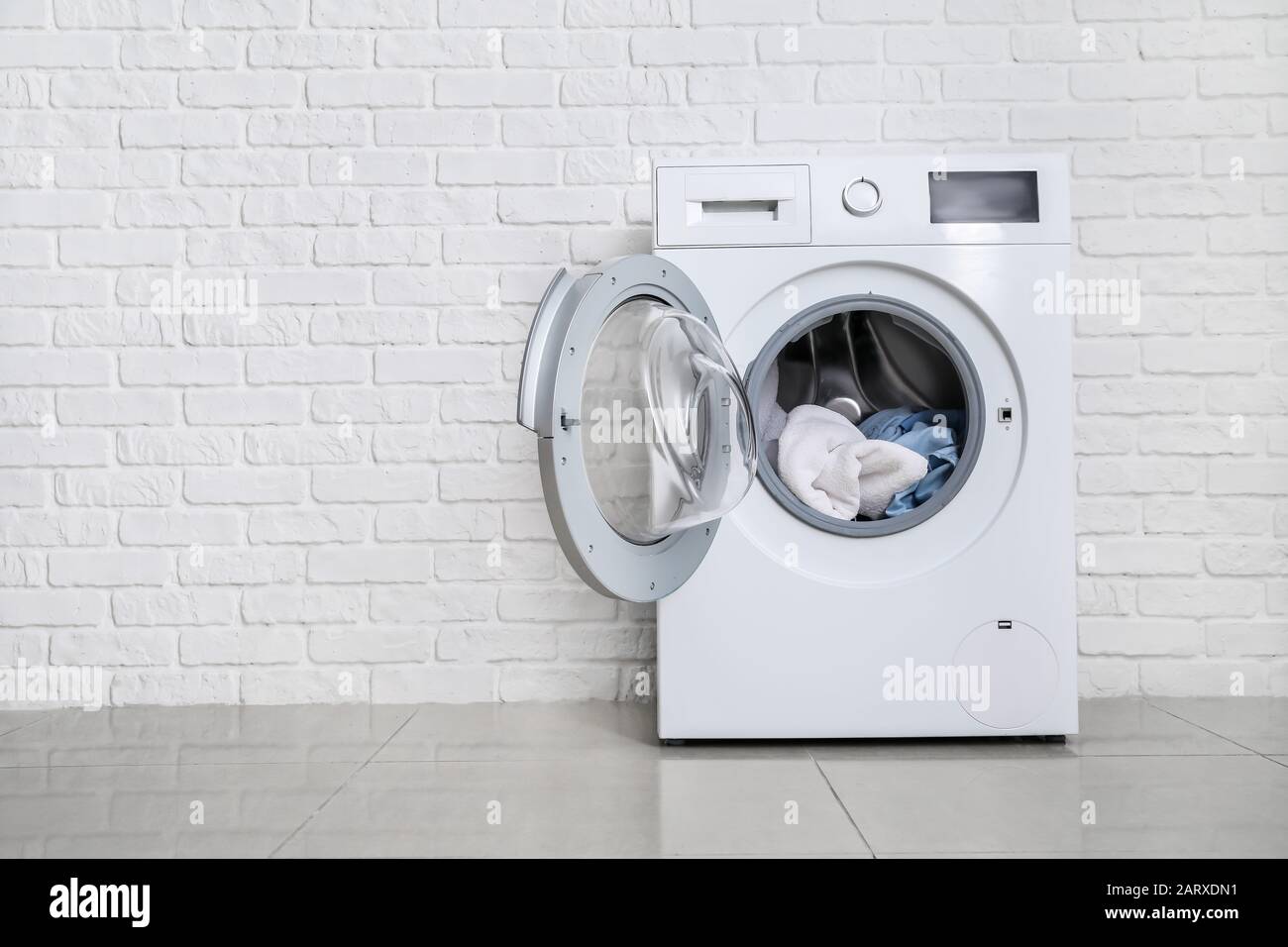 Modern washing machine with laundry near white brick wall Stock Photo ...