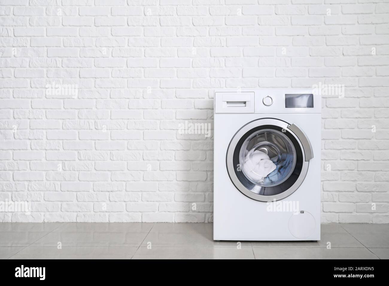 Modern washing machine with laundry near white brick wall Stock Photo ...