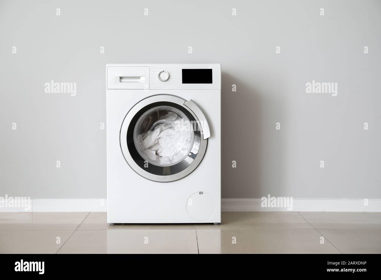 Modern washing machine with laundry near white wall Stock Photo - Alamy