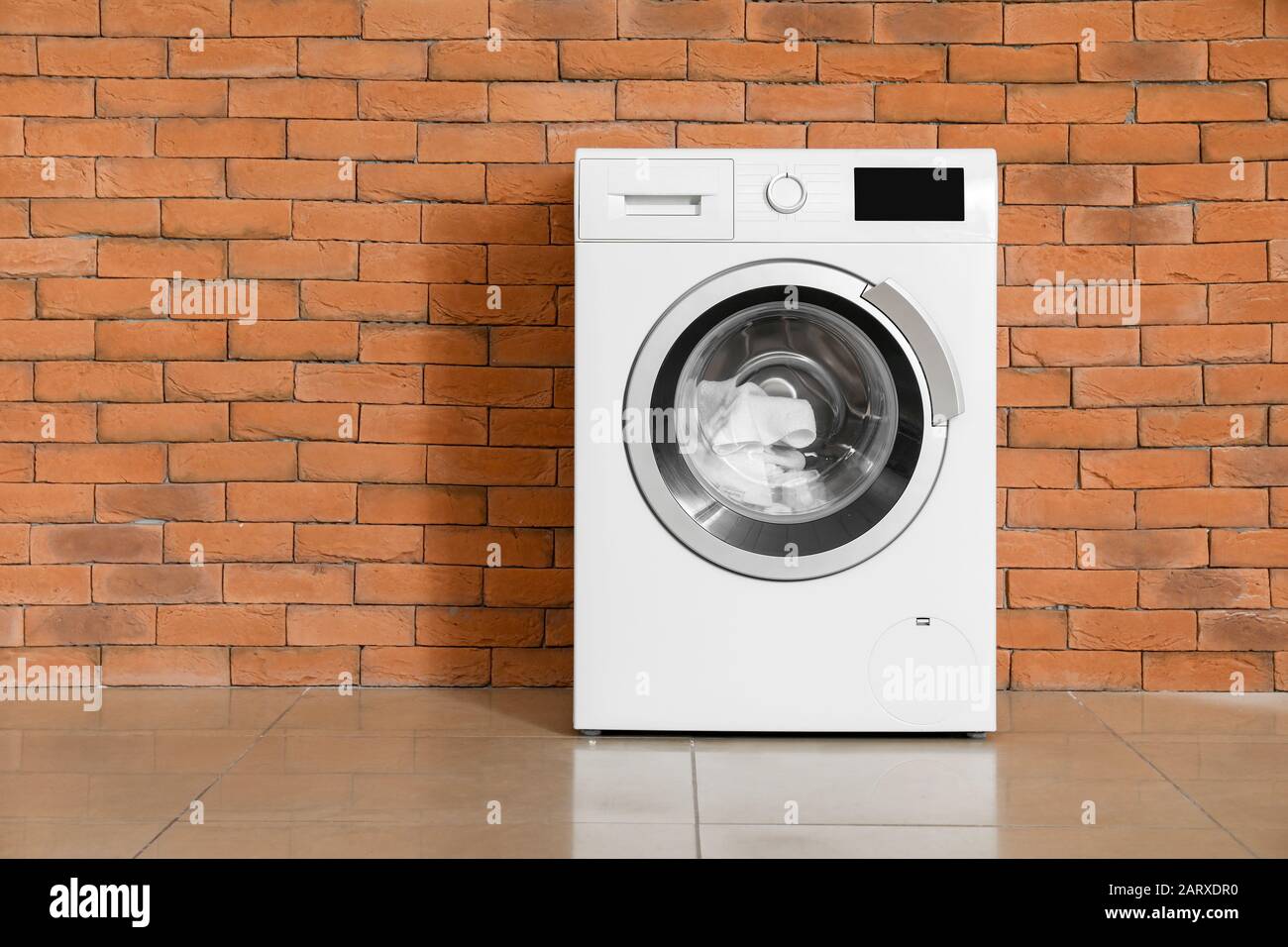 Modern washing machine with laundry near brick wall Stock Photo - Alamy
