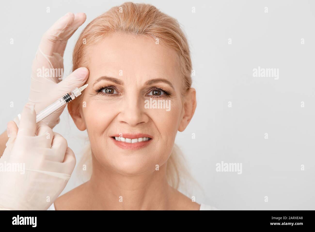 Mature woman receiving anti-aging injection in her face against light ...