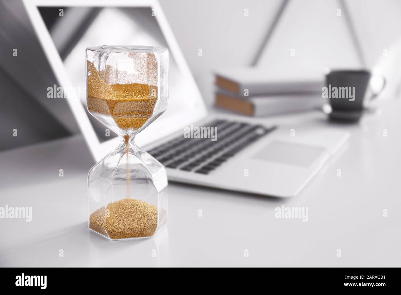 Hourglass and laptop on table in room Stock Photo - Alamy