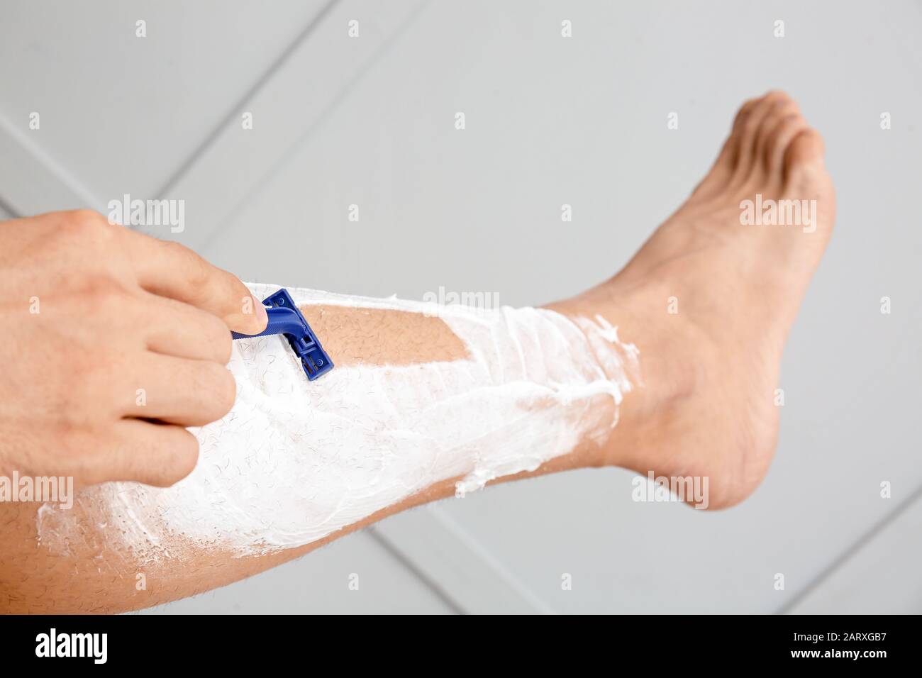 Handsome young man shaving leg on light background Stock Photo - Alamy