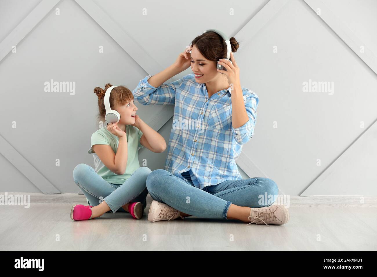 Portrait of happy mother and daughter listening to music on grey ...