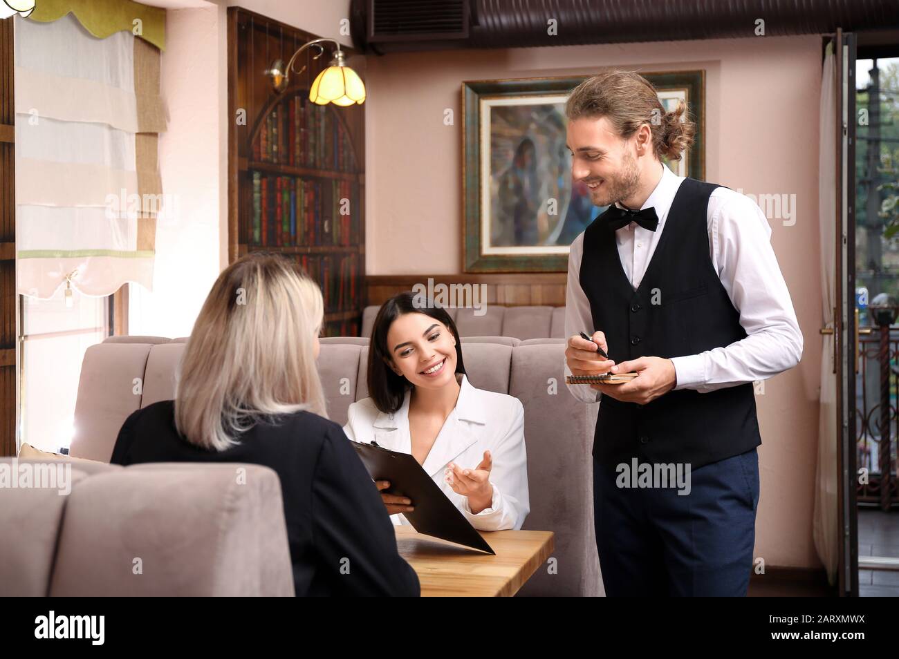 Waiter serving clients in restaurant Stock Photo - Alamy
