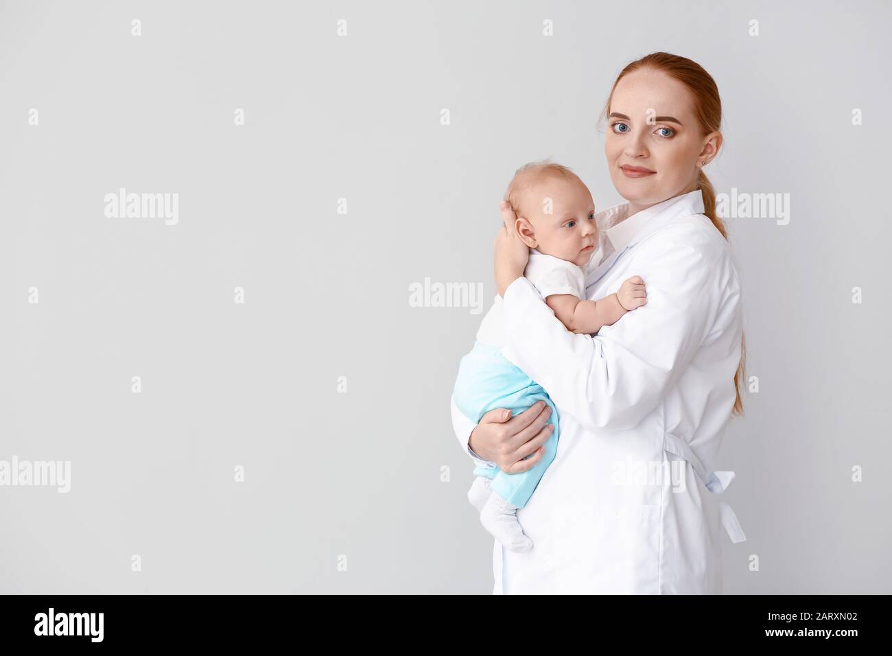 Pediatrician with cute baby on light background Stock Photo - Alamy