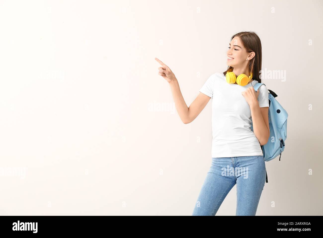 Beautiful female student pointing at something on white background ...