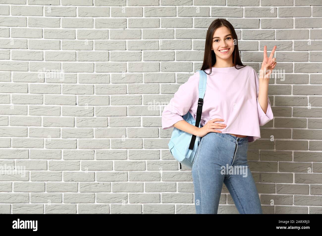 Beautiful female student showing victory gesture on brick background ...