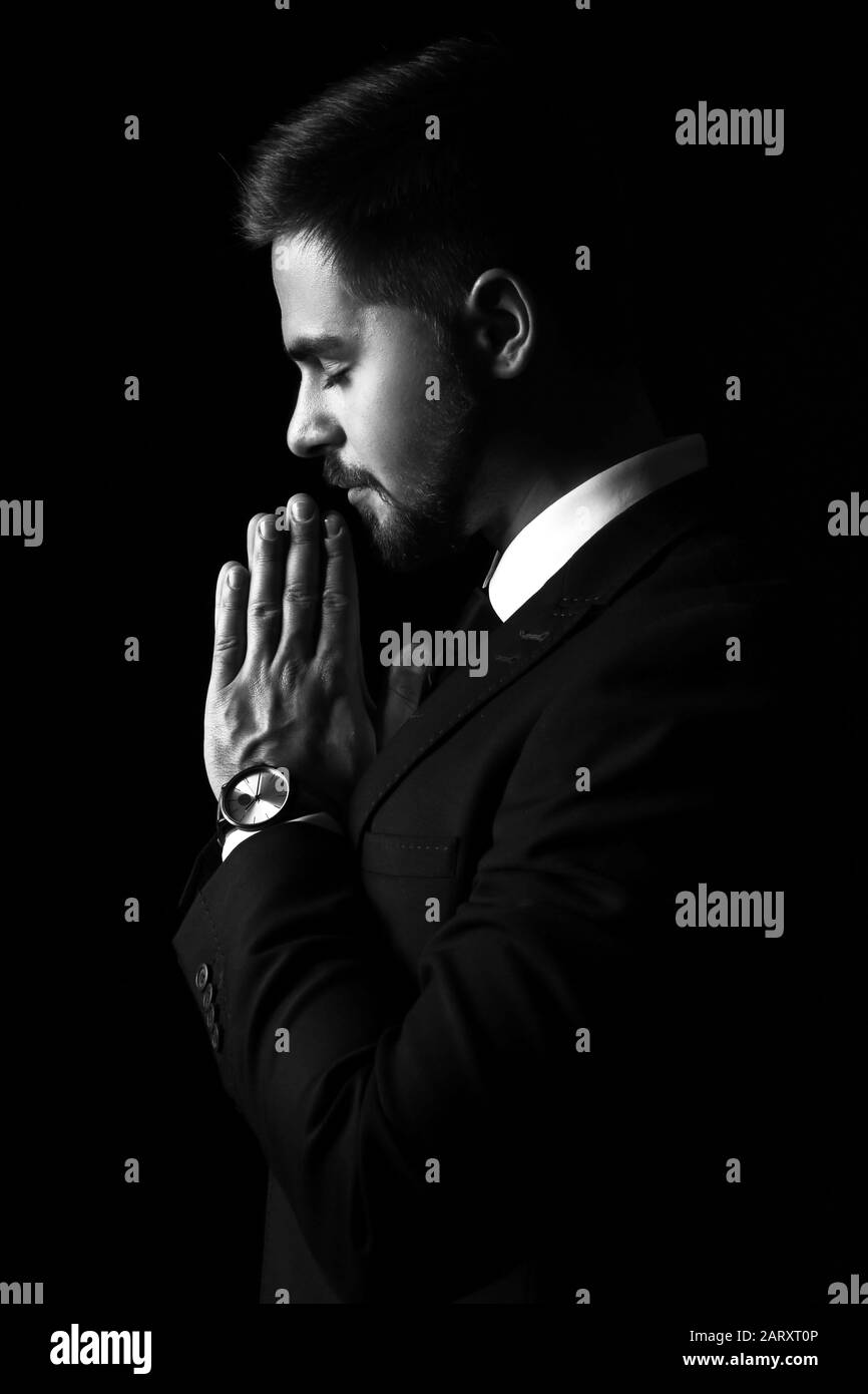 Black and white portrait of handsome praying businessman on dark ...