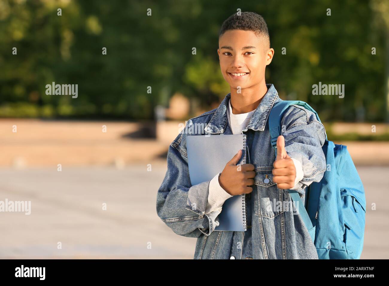 Portrait of teenage African-American student showing thumb-up outdoors ...
