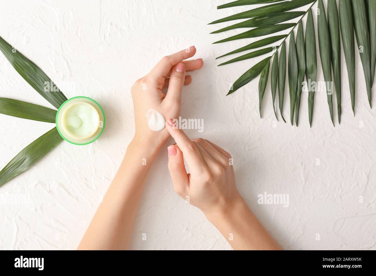 Young woman applying hand cream at light table Stock Photo - Alamy