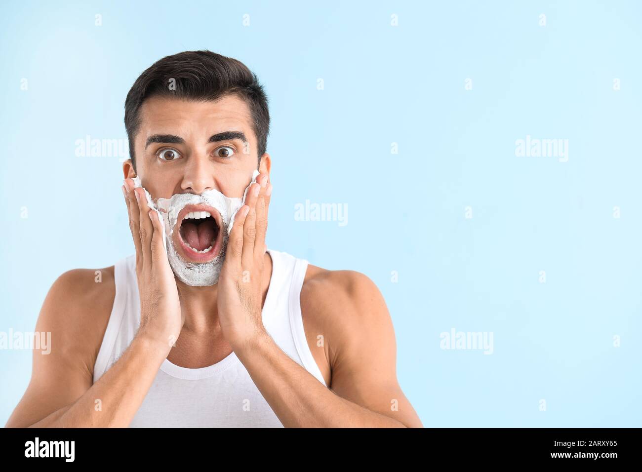 Screaming young man with shaving foam on his face against color ...